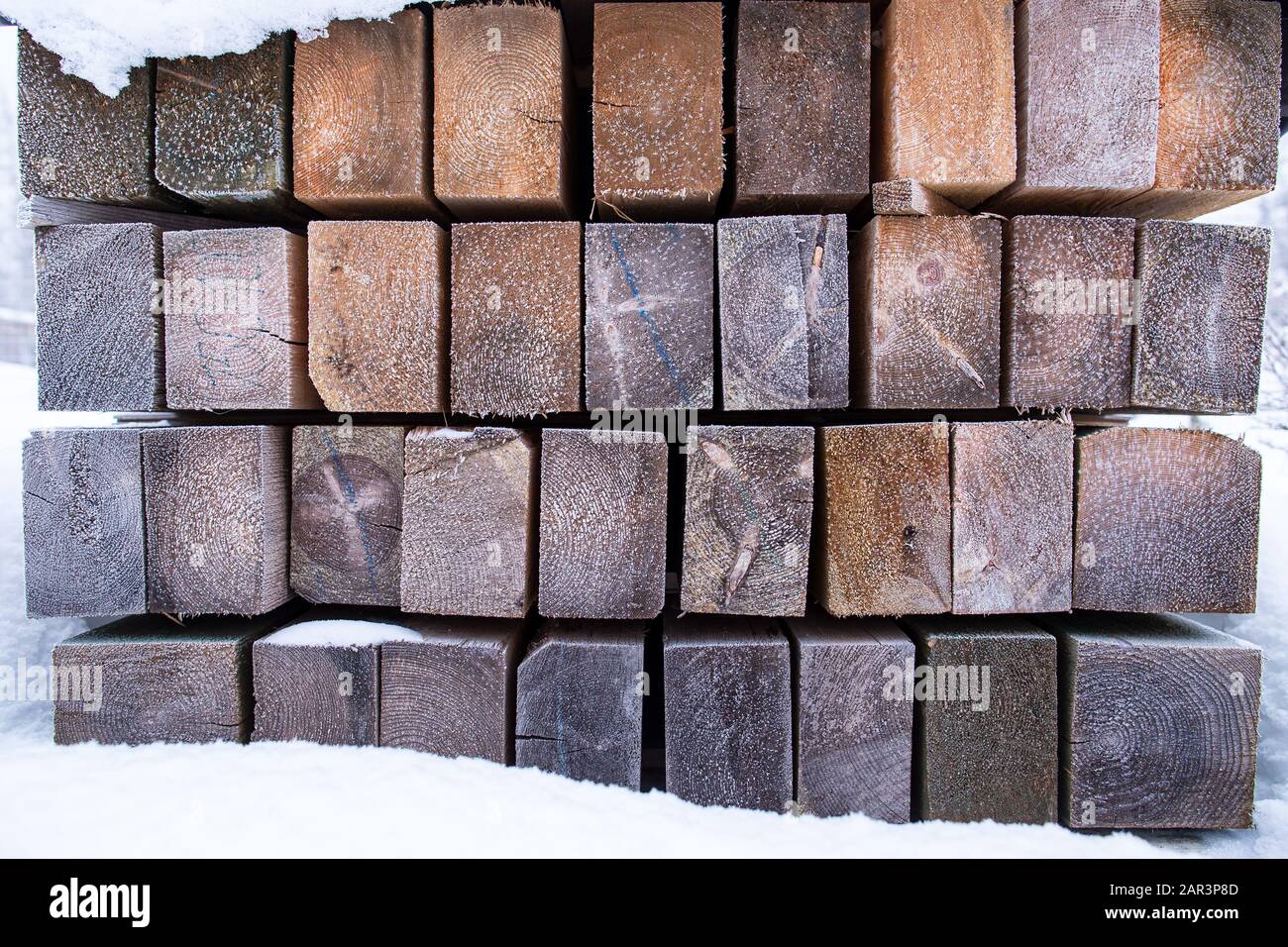 Stacked wooden timber, covered with hoarfrost and snow, in a rustic ...