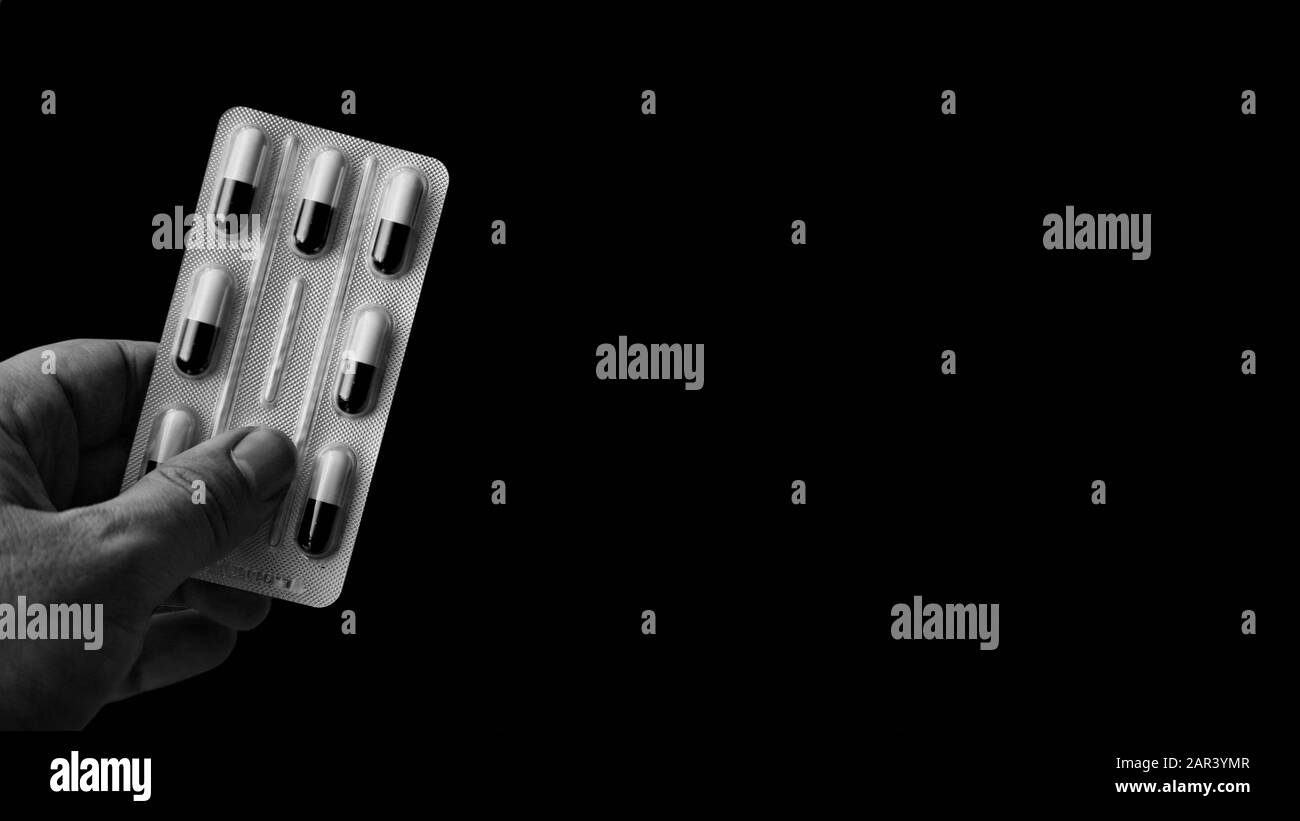 Grey scale shot of a person holding a pack of capsules with a black ...