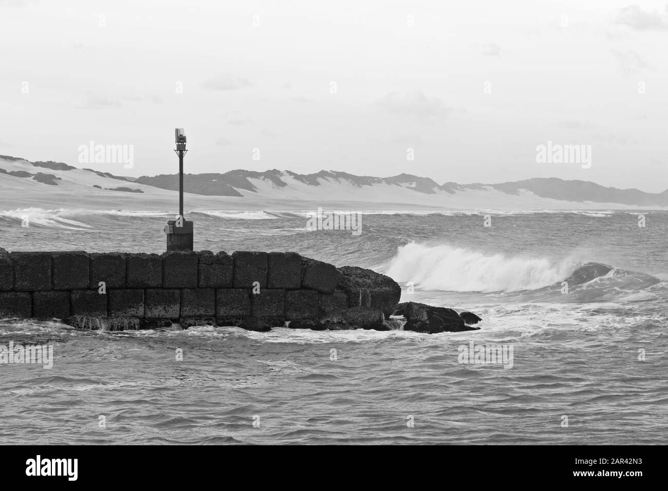 Grey scale shot of the ocean waves breaking at the beautiful stone pier ...