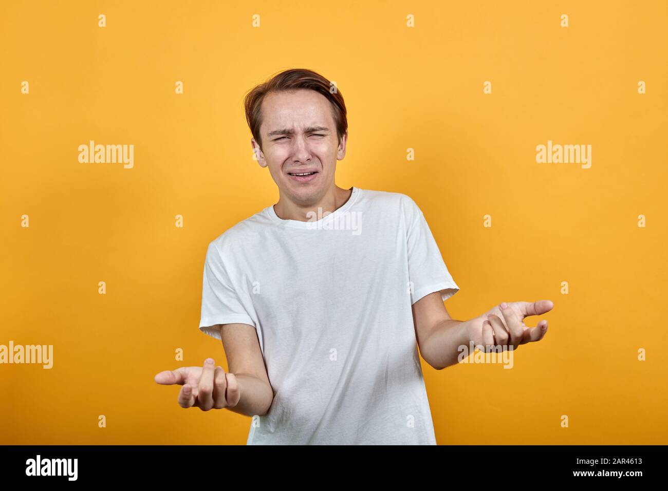 Upset crying man in white shirt on yellow background gesturing with his ...