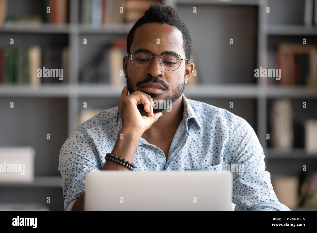 Serious thoughtful african businessman looking at laptop thinking ...