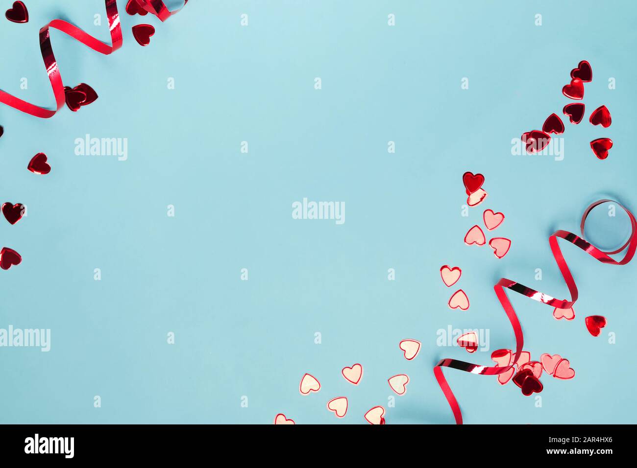 Red heart shaped confetti and curly ribbons on blue background with ...