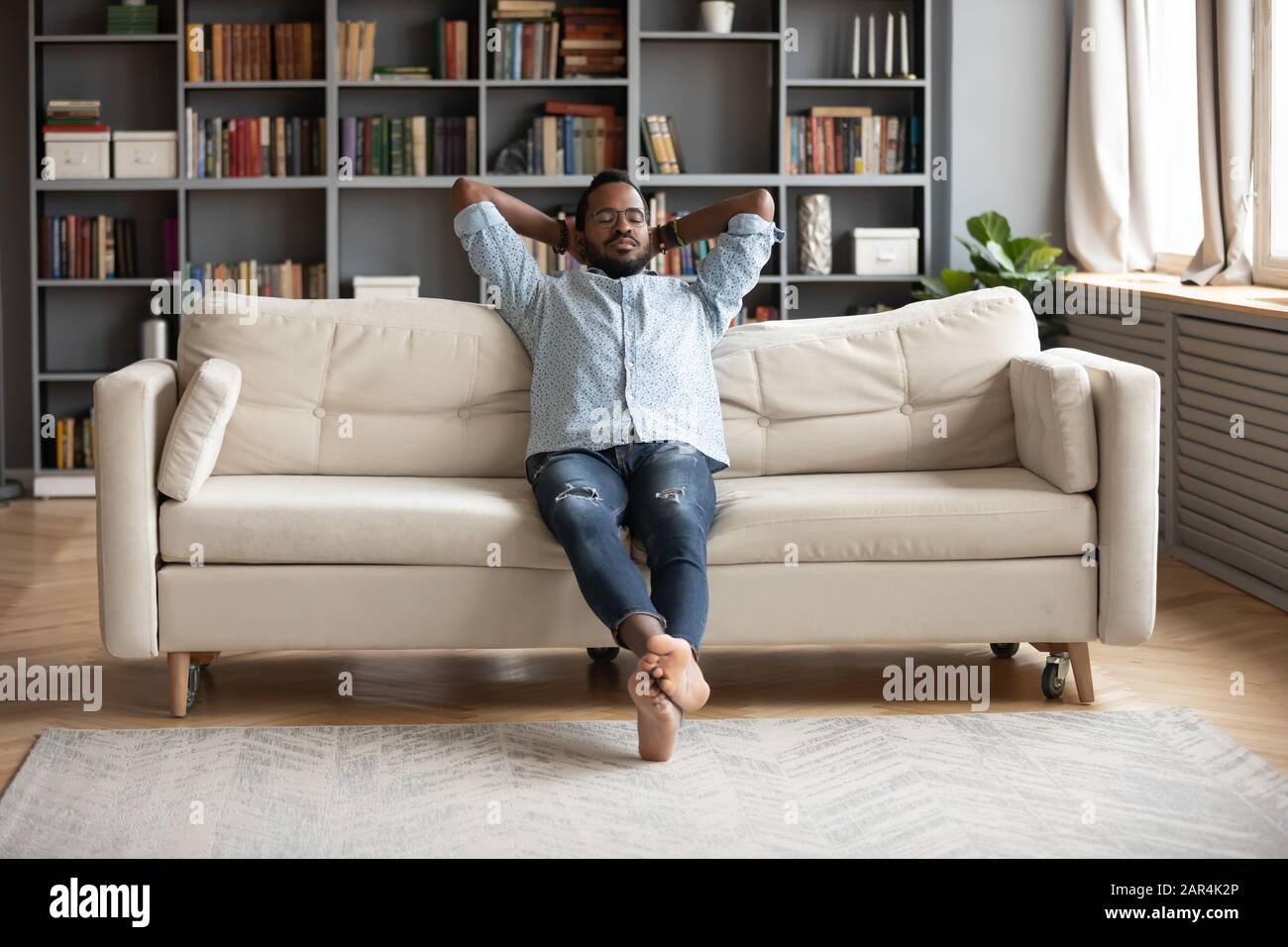 Serene barefoot african man resting on sofa hands behind head Stock ...