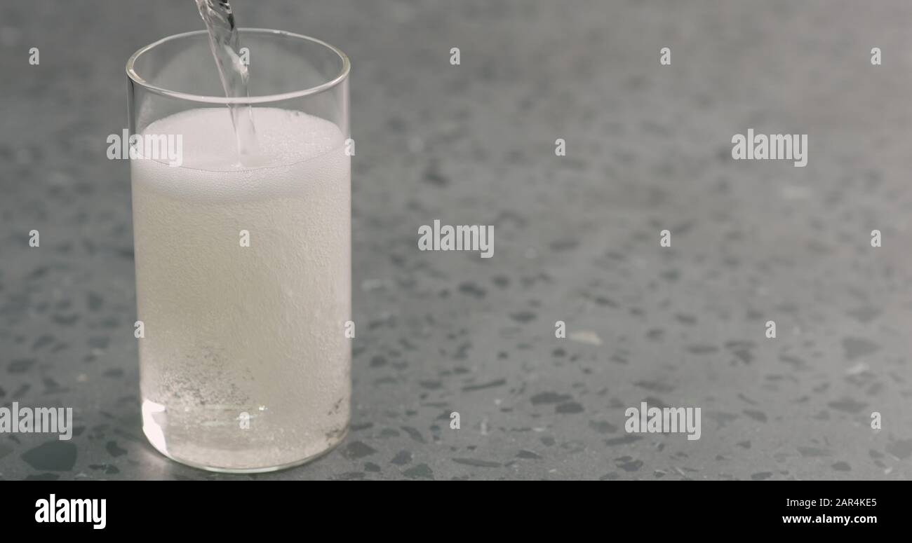 pour transparent sparkling drink in glass on terrazzo surface with copy ...