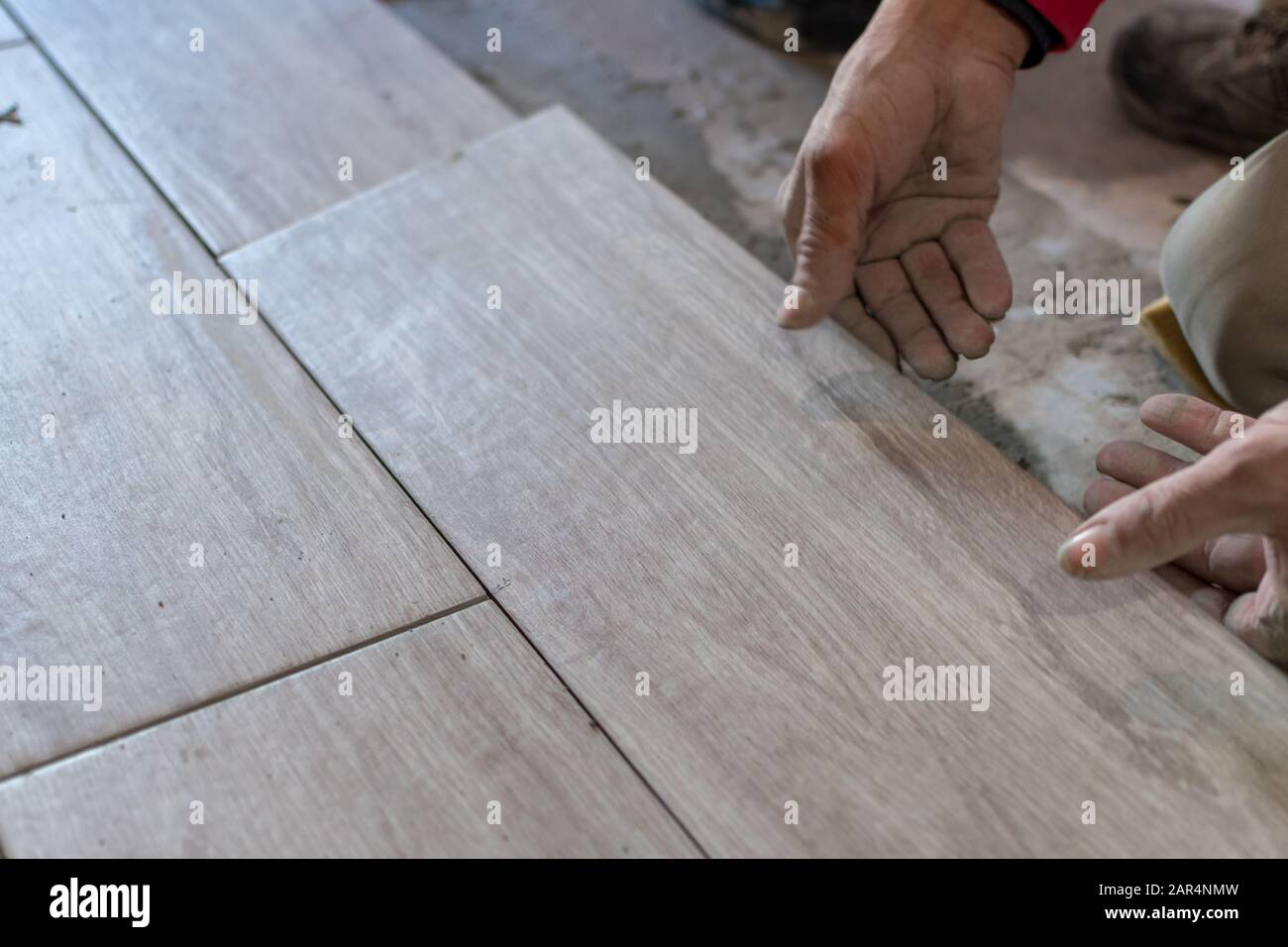 Man installing rectangular shaped floor tiles in kitchen. Applying ...