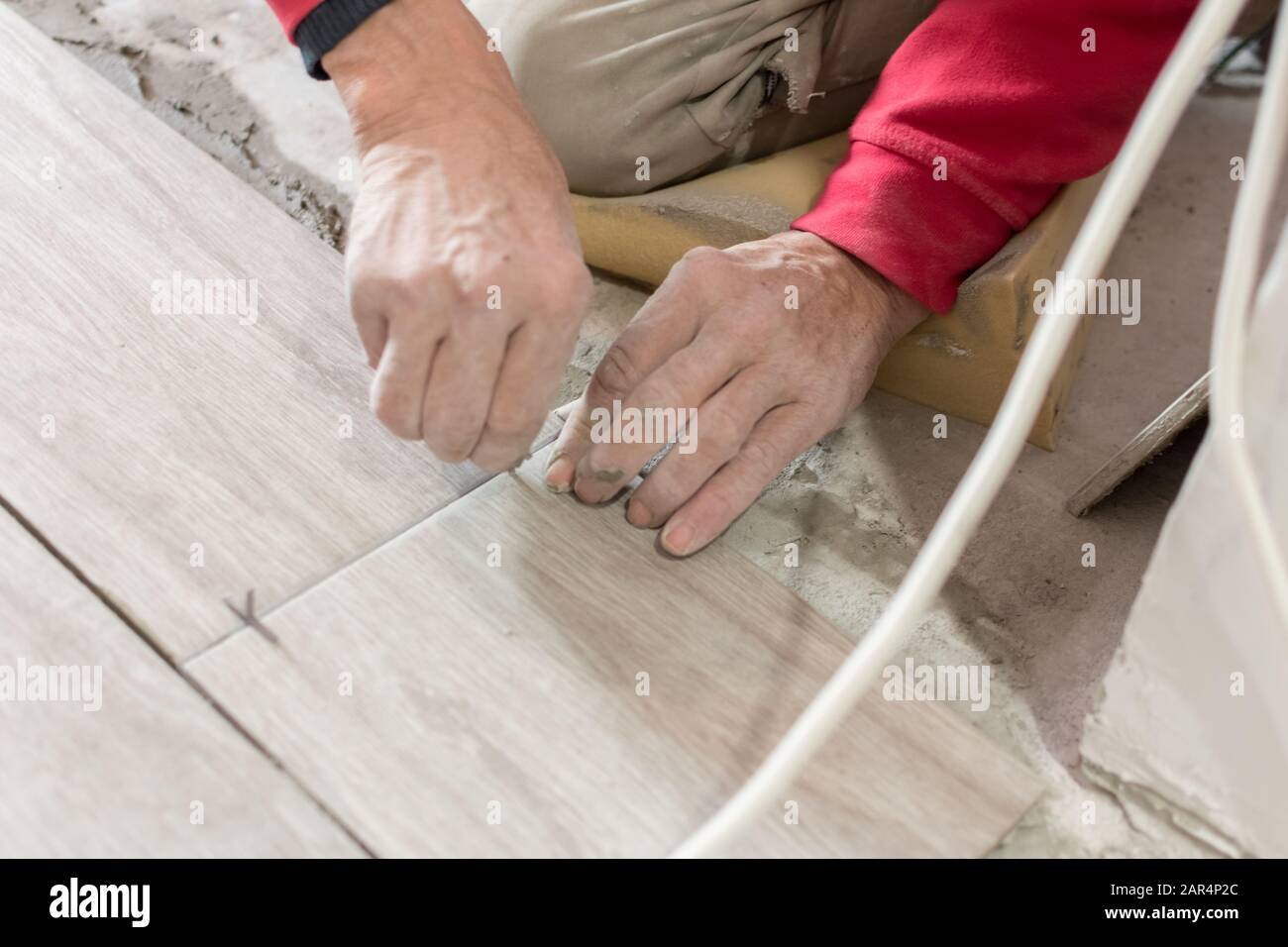 Man installing rectangular shaped floor tiles in kitchen. Applying adhesive before installation ...