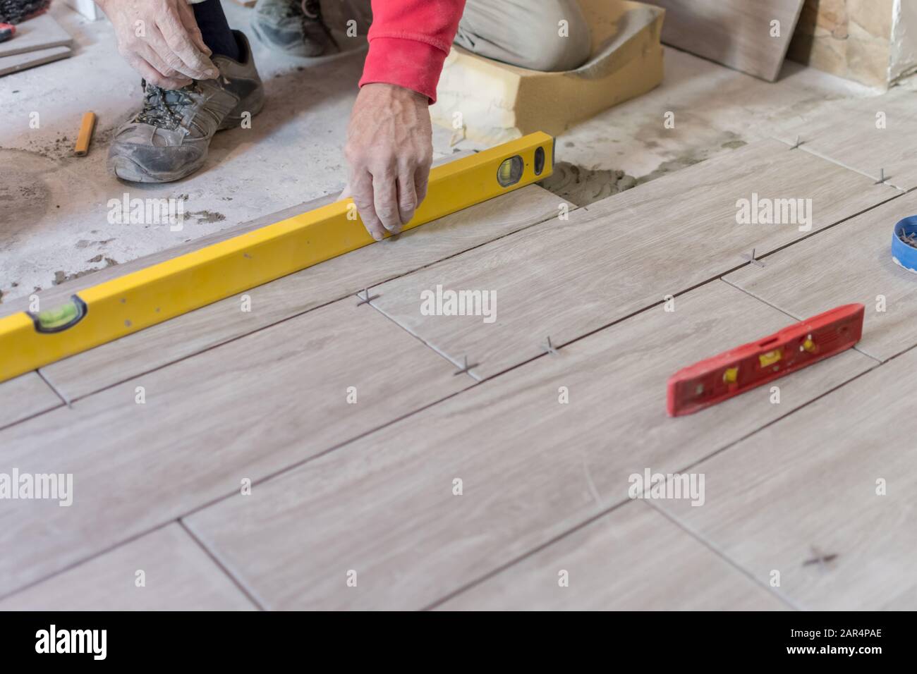 Man installing rectangular shaped floor tiles in kitchen. Applying adhesive before installation ...