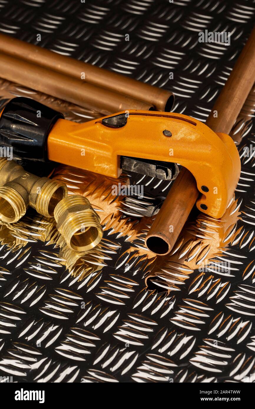 Copper pipe and cutter with plumbing connectors on a steel checker ...