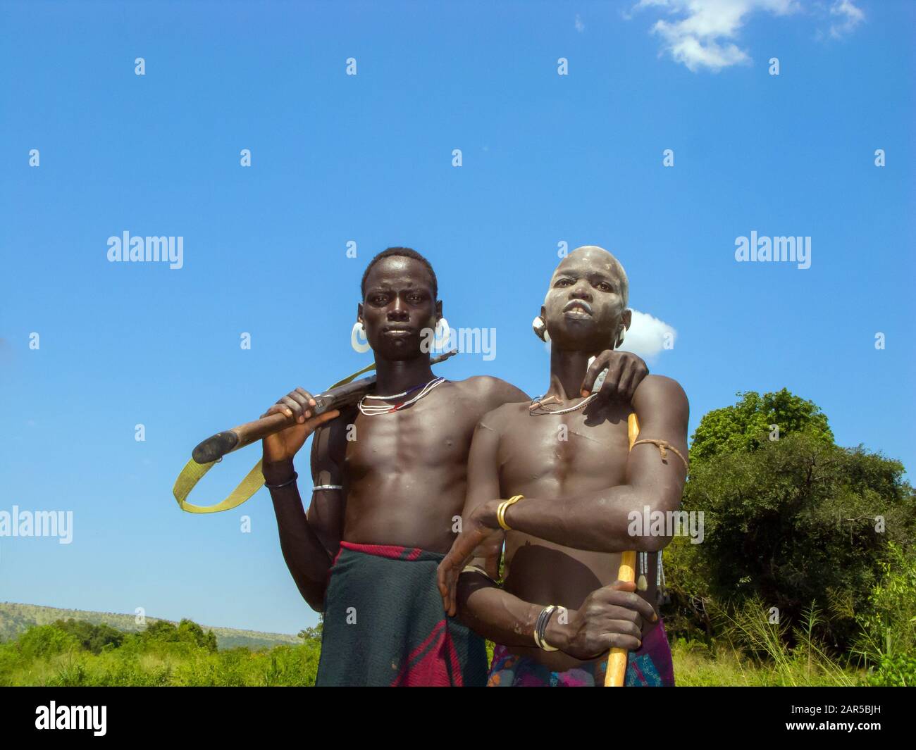 Portrait of two young Mursi warriors holding a stick. The Mursi (or ...