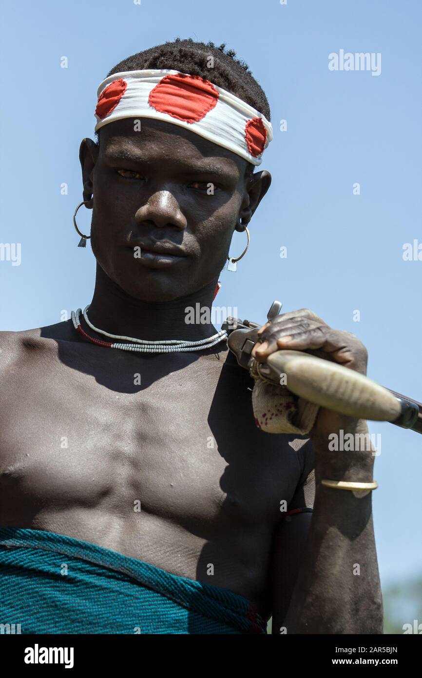 Portrait of young Mursi warrior holding a gun. The Mursi (or Murzu) are ...