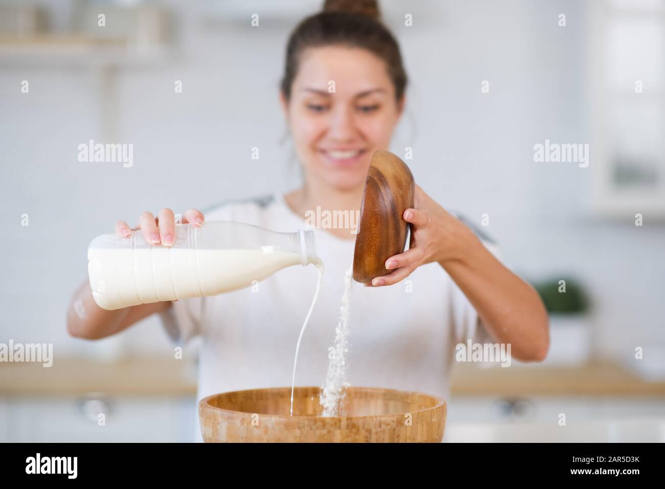 girl pouring milk and pour flour into a wooden cup for making dough ...