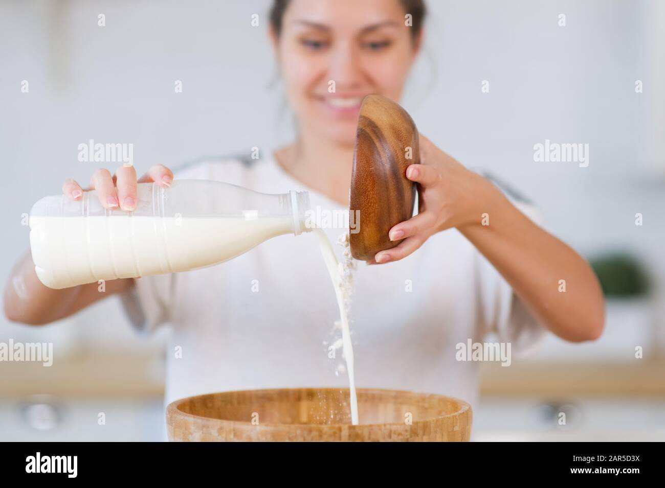 girl pouring milk and pour flour into a wooden cup for making dough ...