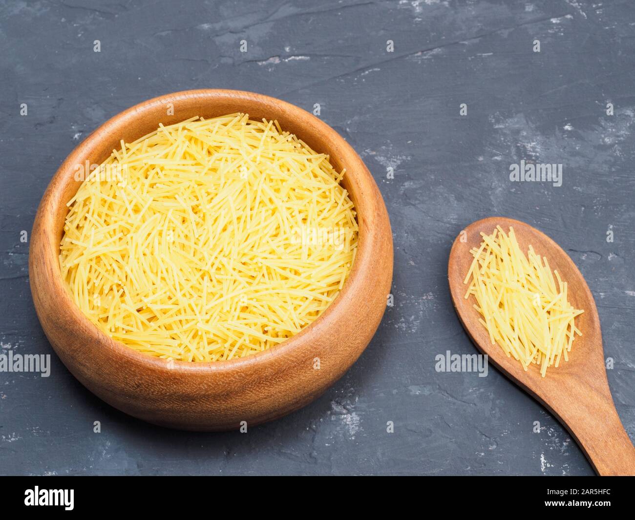 Small pasta in wooden bowl and spoon on a black concrete background ...