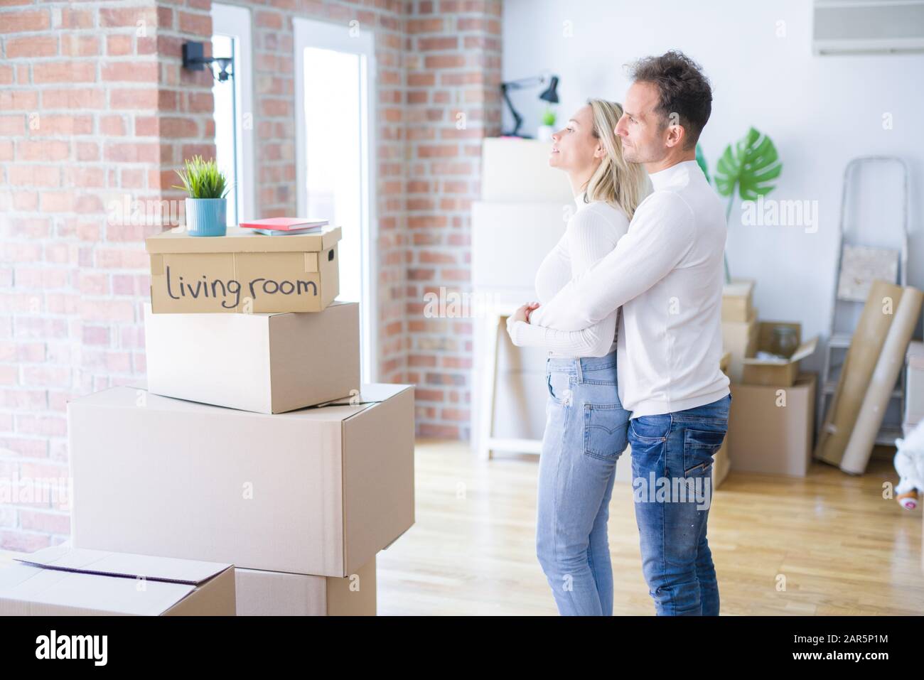 Young beautiful couple standing at new home around cardboard boxes ...