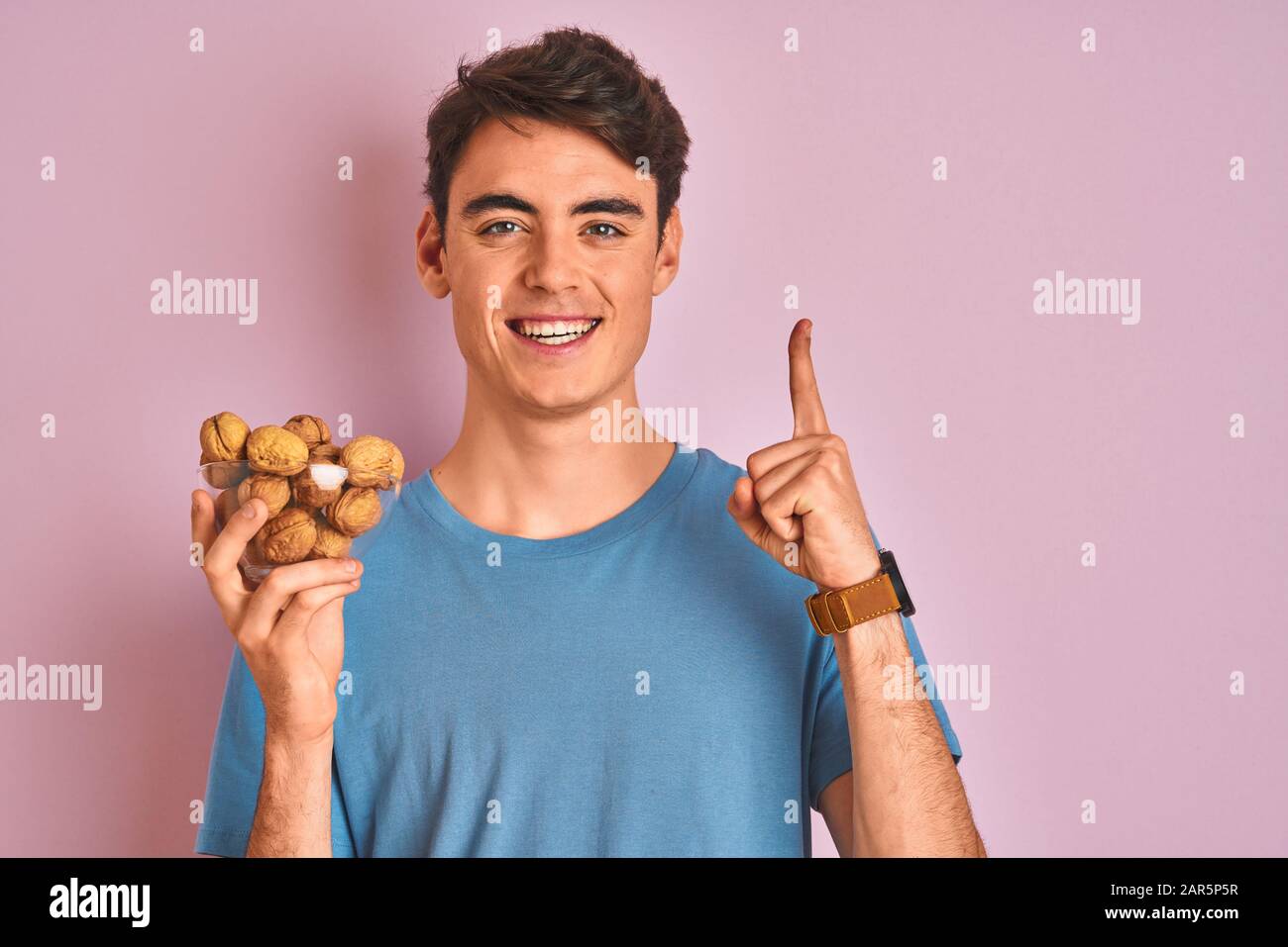 Teenager boy holding bunch of natural walnuts over pink isolated ...