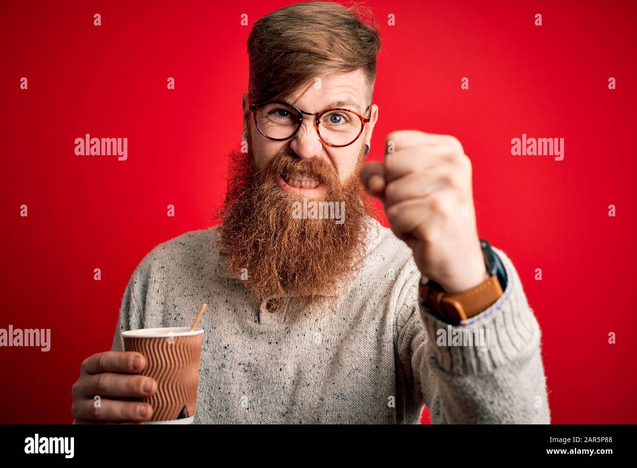 Irish Redhead Man With Beard Drinking A Takeaway Coffee On A Paper Cup Over Red Background