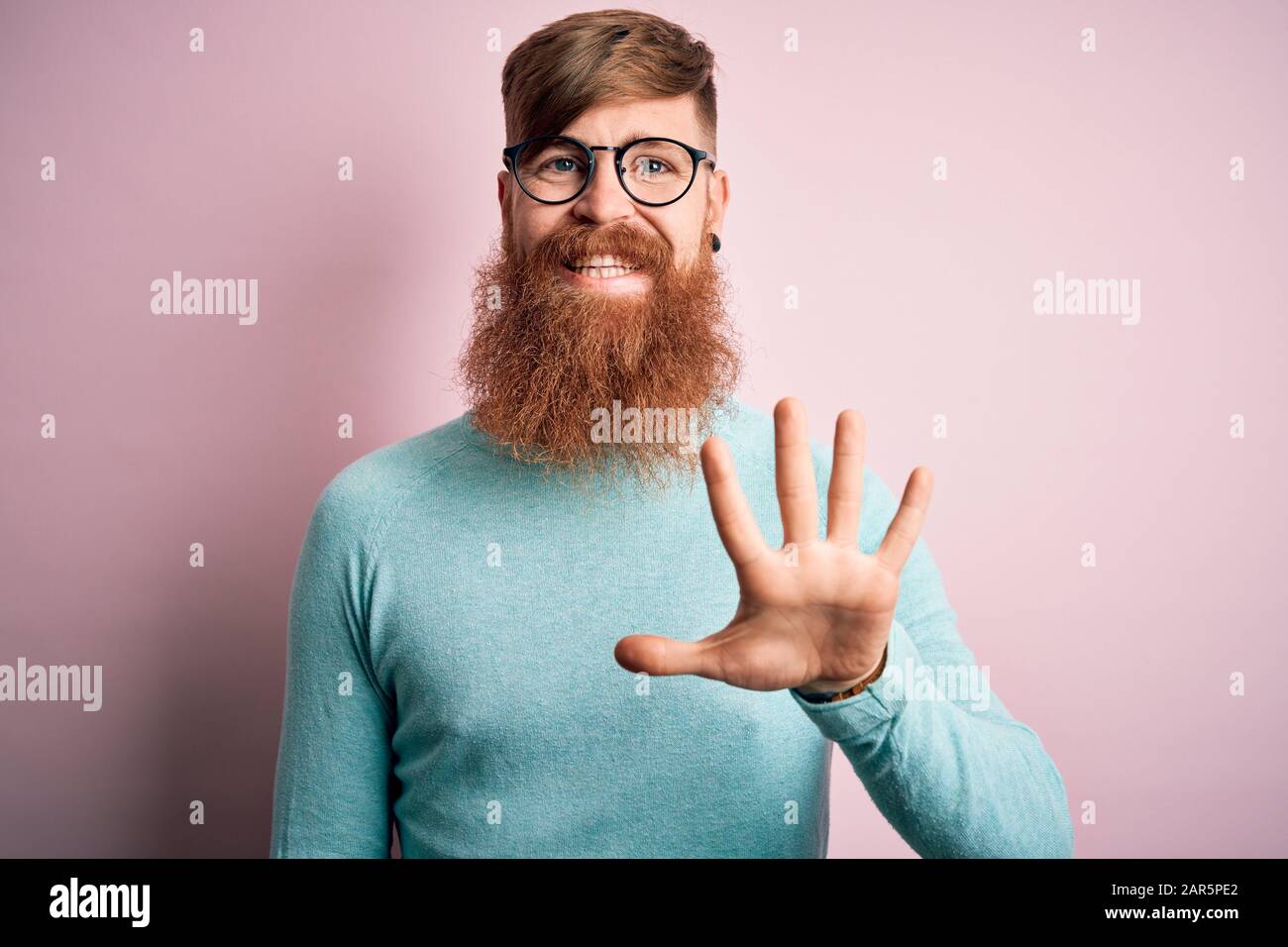Handsome Irish redhead man with beard wearing glasses over pink ...