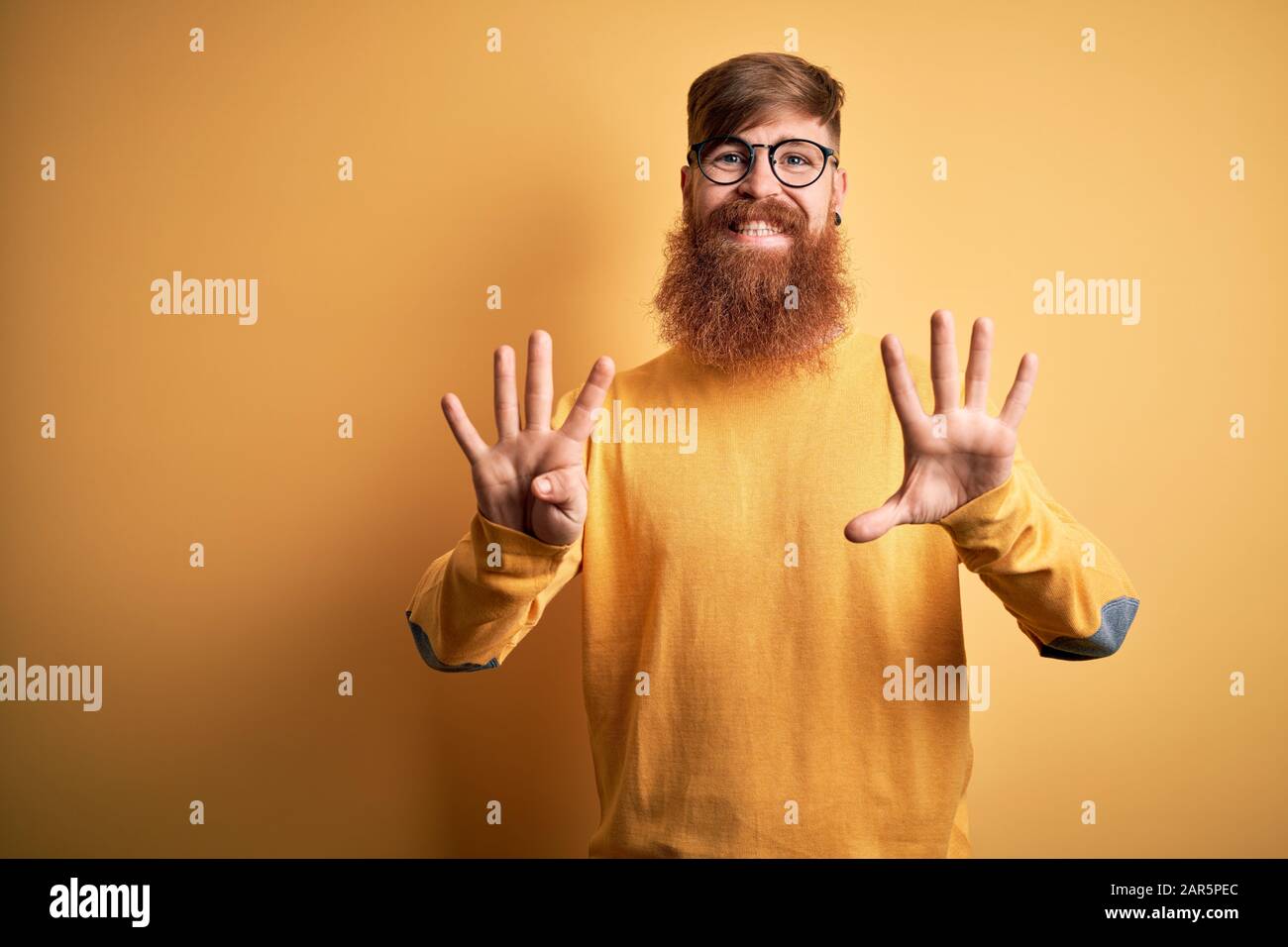 Handsome Irish redhead man with beard wearing glasses over yellow ...