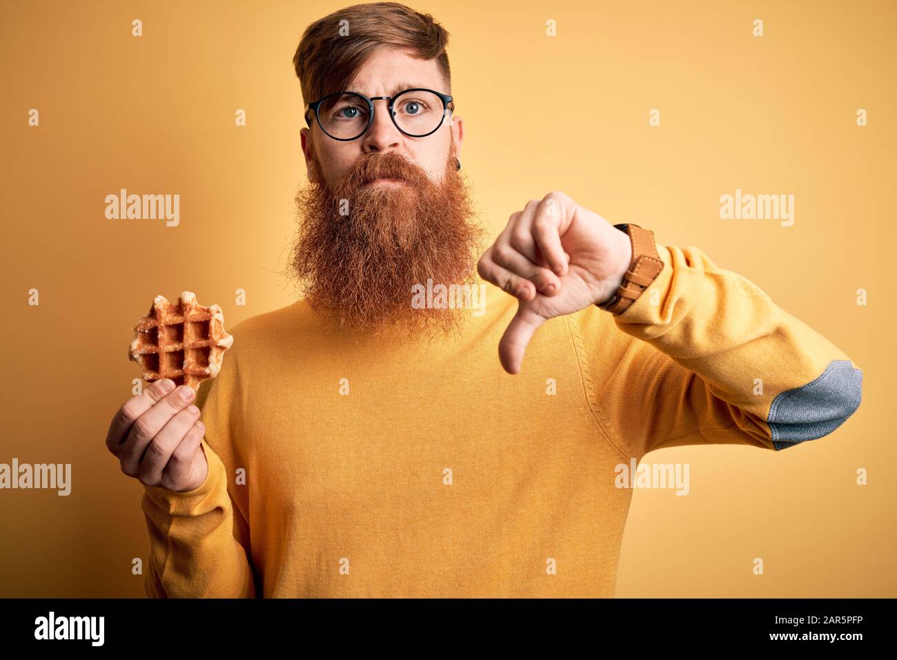 Redhead Irish Man With Beard Eating Sweet Belgian Waffle Pastry Over Yellow Background With