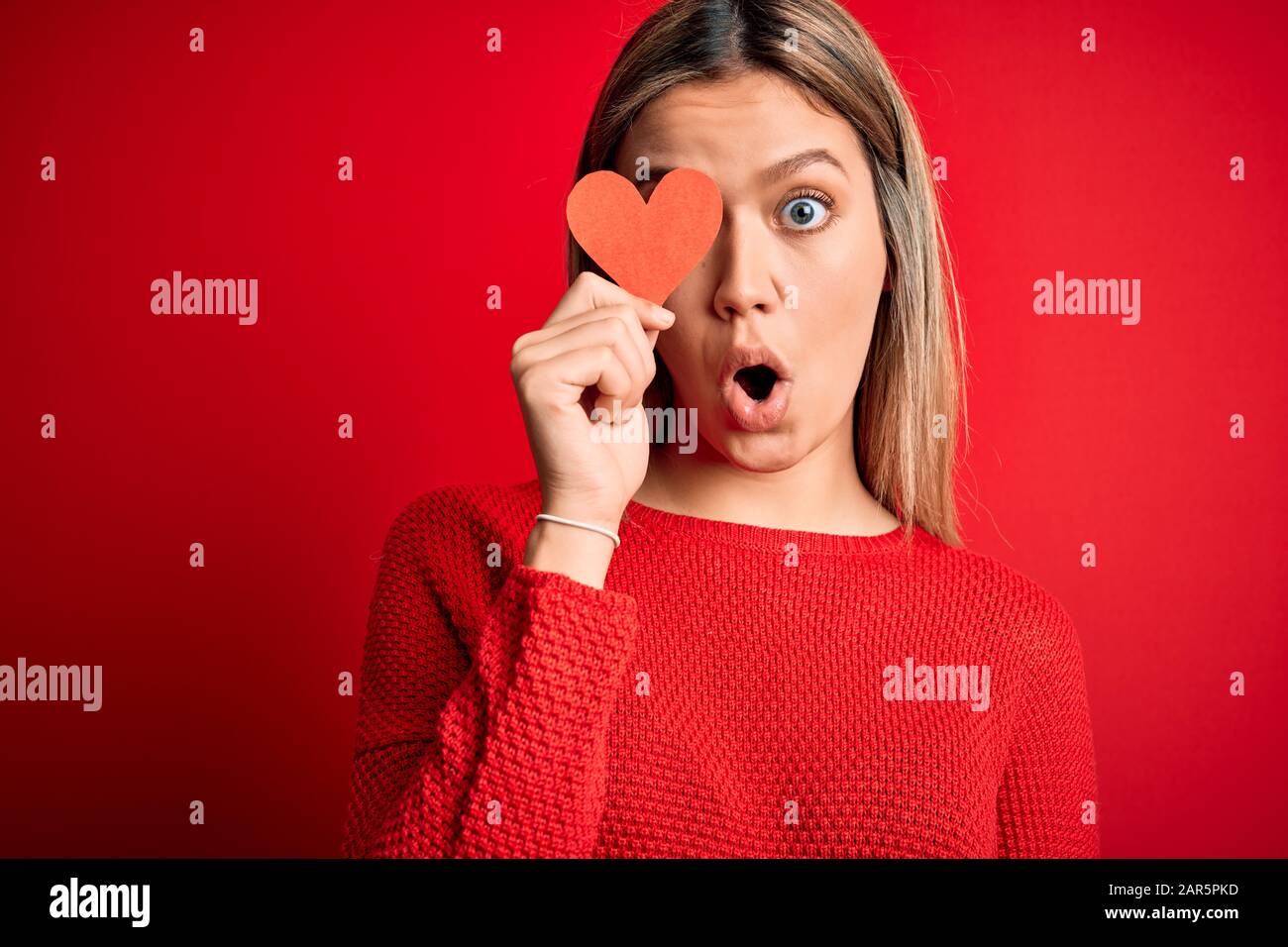 Young beautiful woman holding heart card standing over isolated red ...