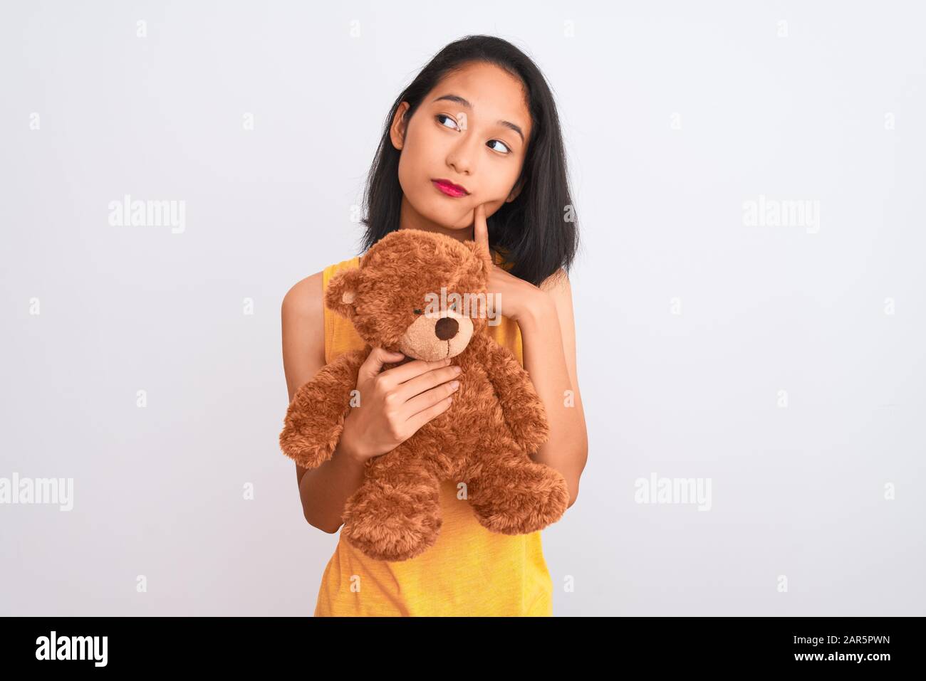 Young beautiful chinese woman holding teddy bear standing over isolated ...