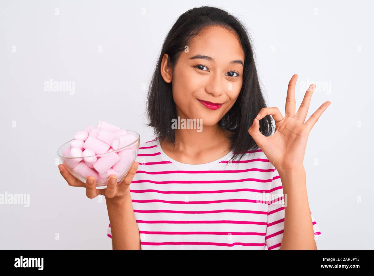 Beautiful chinese woman holding bowl with marshmallows over isolated ...