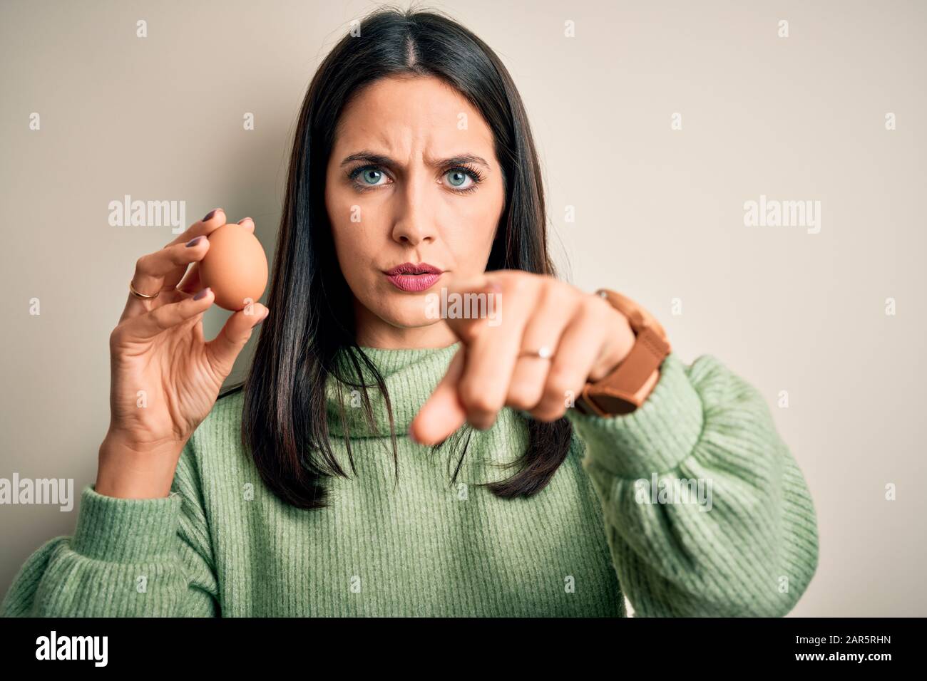Young brunette woman with blue eyes holding fresh raw egg over isolated ...