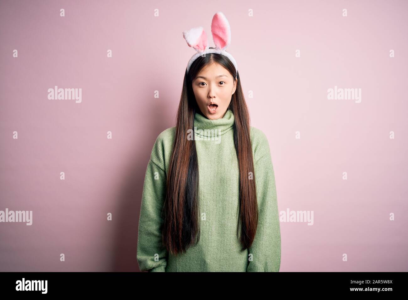 Young asian woman wearing cute easter bunny ears over pink background ...