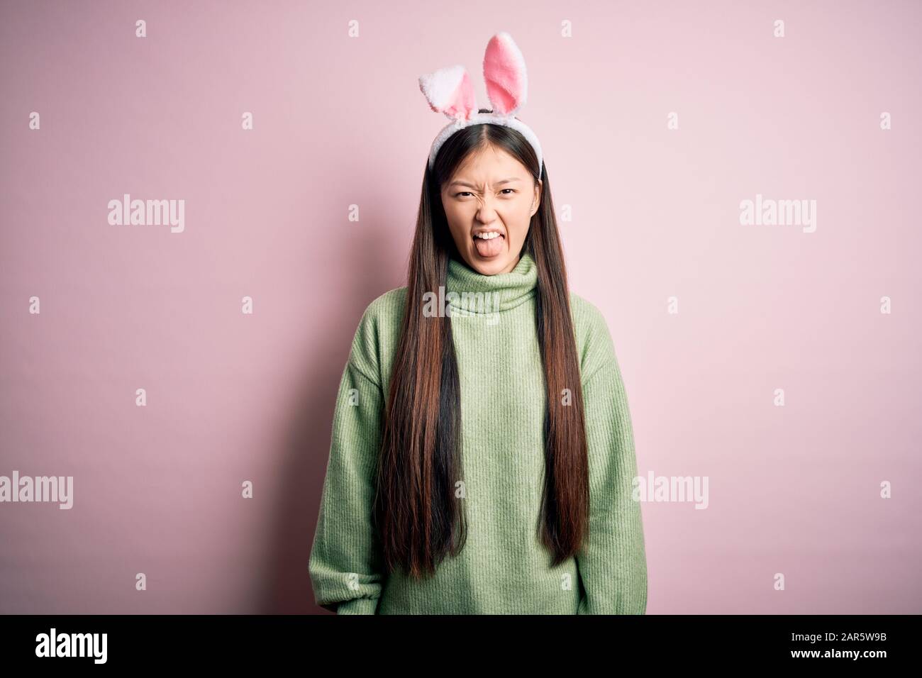Young asian woman wearing cute easter bunny ears over pink background ...