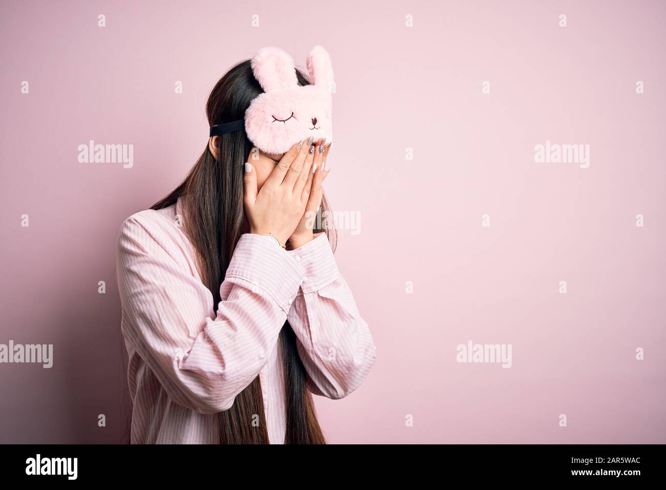 Young asian woman wearing pajama and sleep mask over pink isolated ...