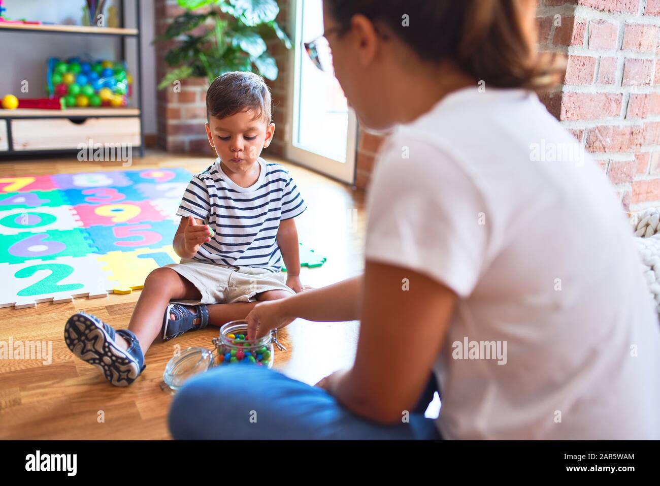 Beautiful teacher and toddler boy sitting eating small chocolate balls ...