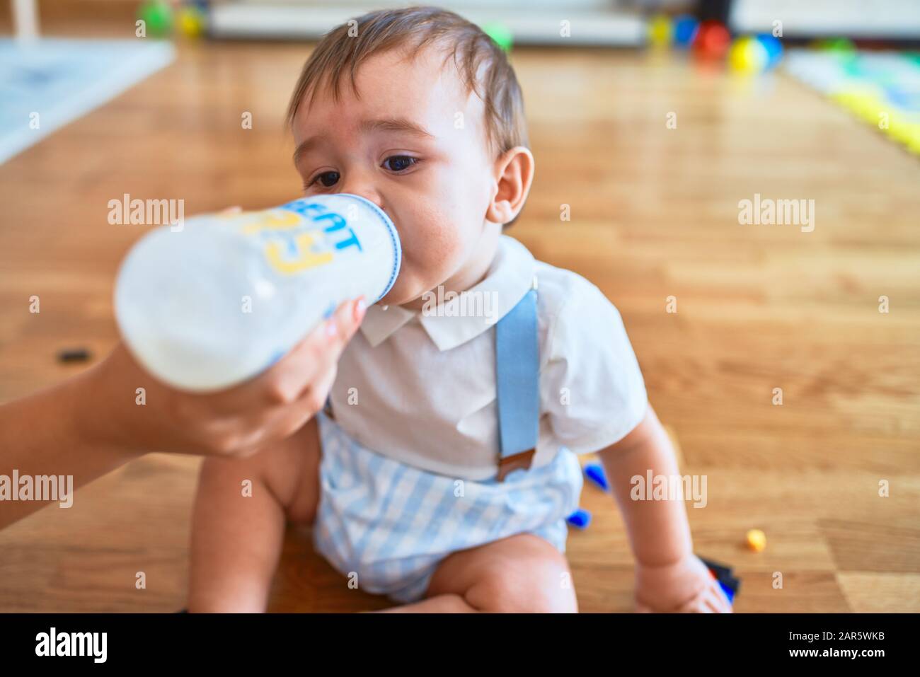 Adorable toddler sitting on the floor drinking milk using feeding ...