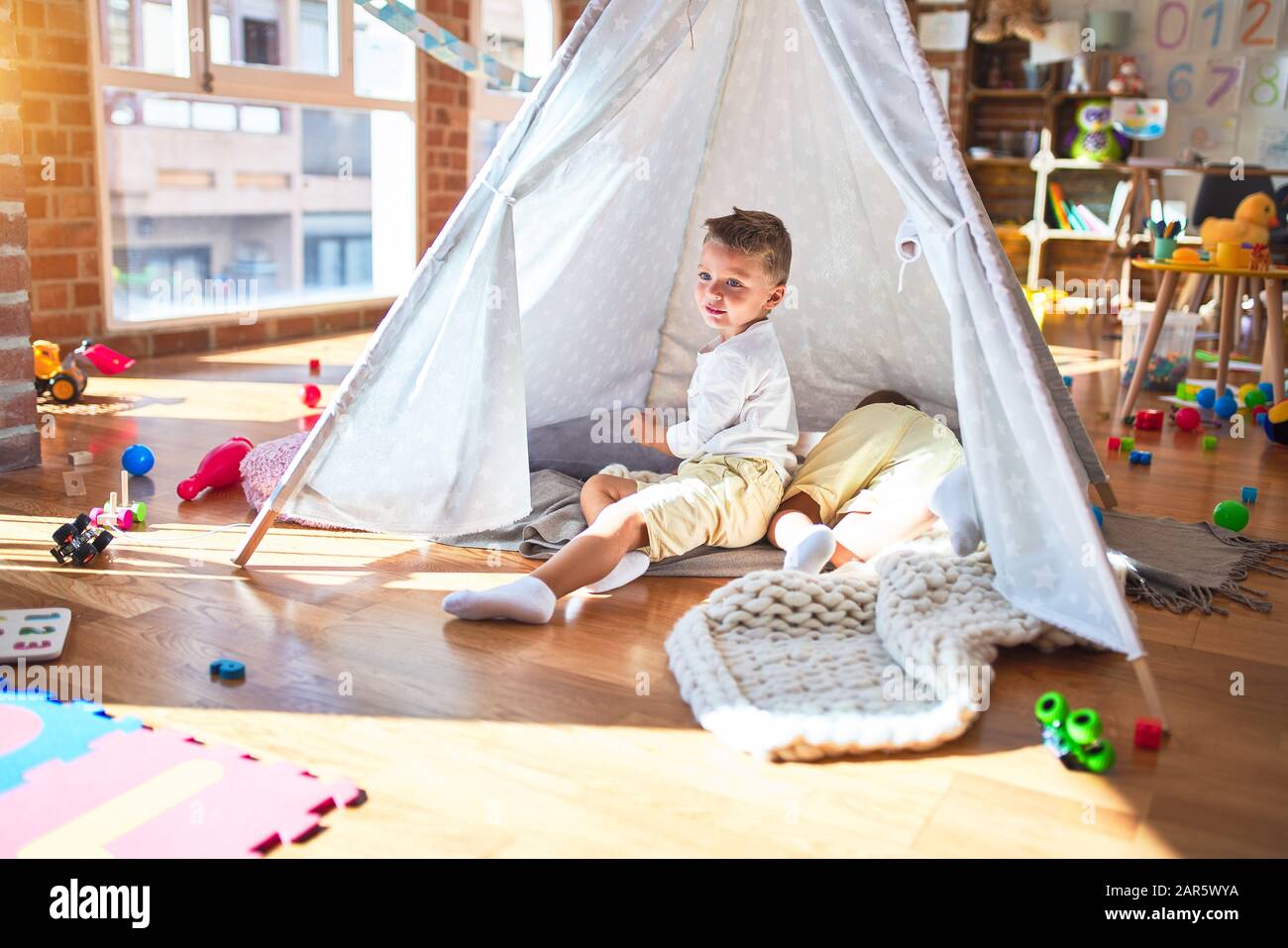 Adorable blonde twins playing inside tipi around lots of toys at ...
