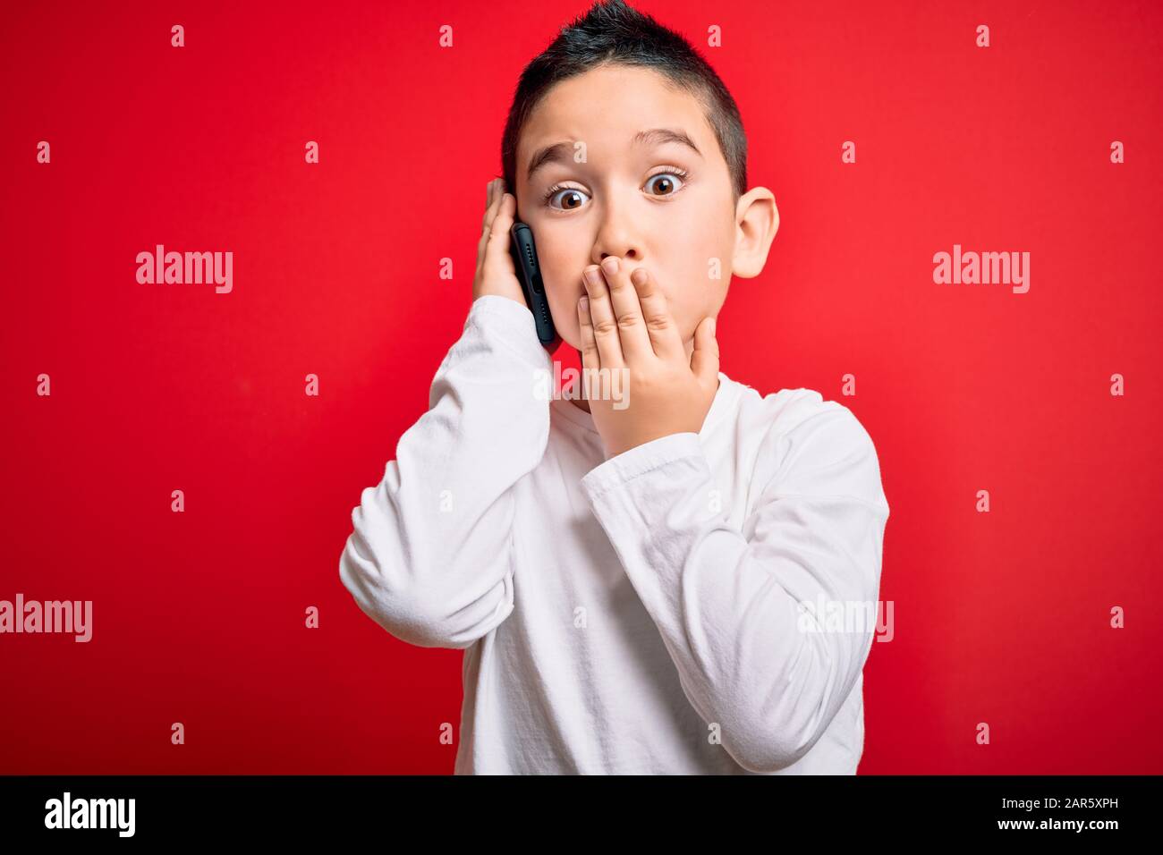 Young little boy kid talking on smartphone mobile over red isolated ...