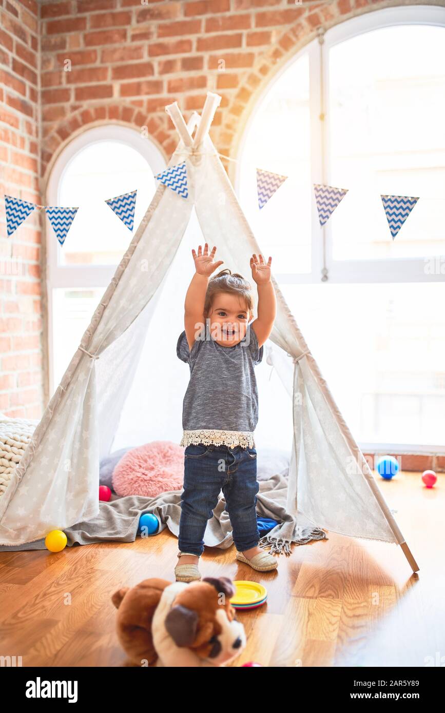 Beautiful toddler standing inside tipi with hands raised smiling at ...