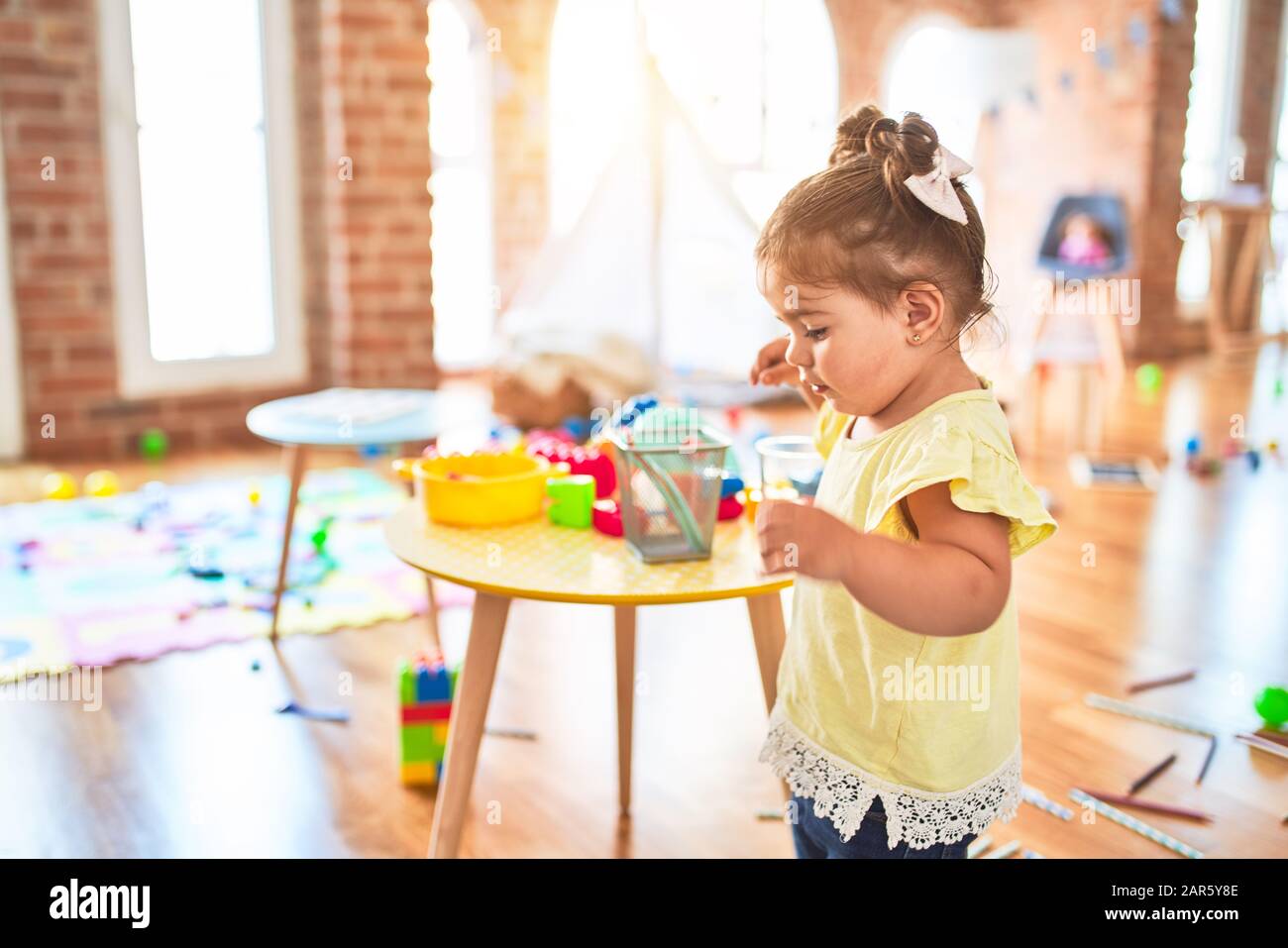 Beautiful toddler standing around lots of toys at kindergarten Stock ...