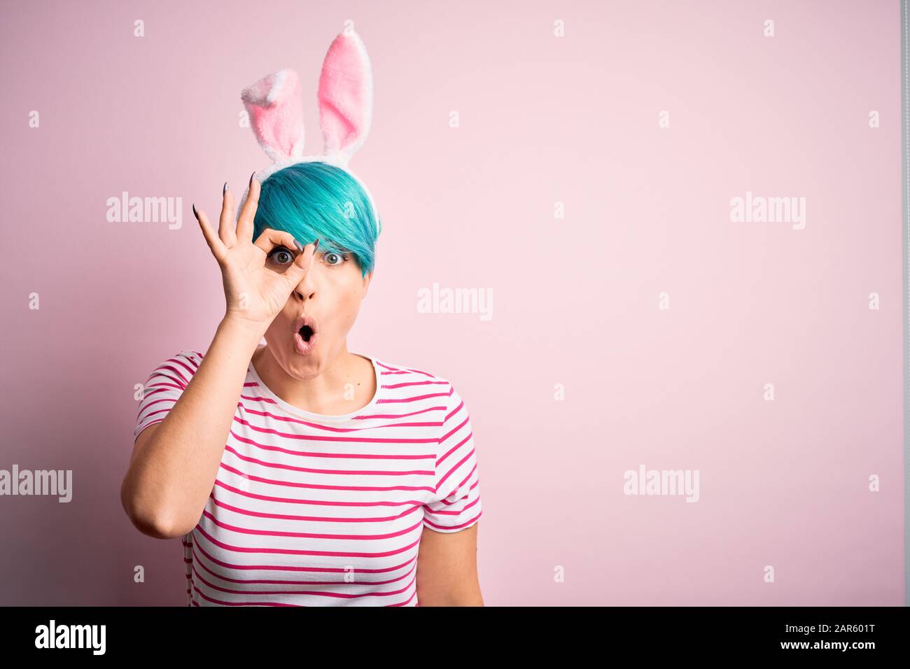 Young woman with fashion blue hair wearing easter rabbit ears over pink ...