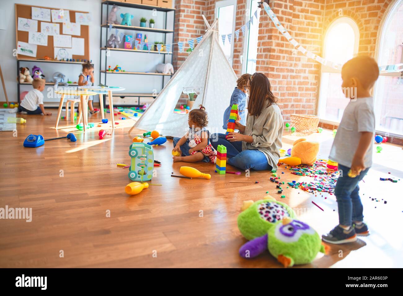 Beautiful teacher and group of toddlers playing around lots of toys at ...