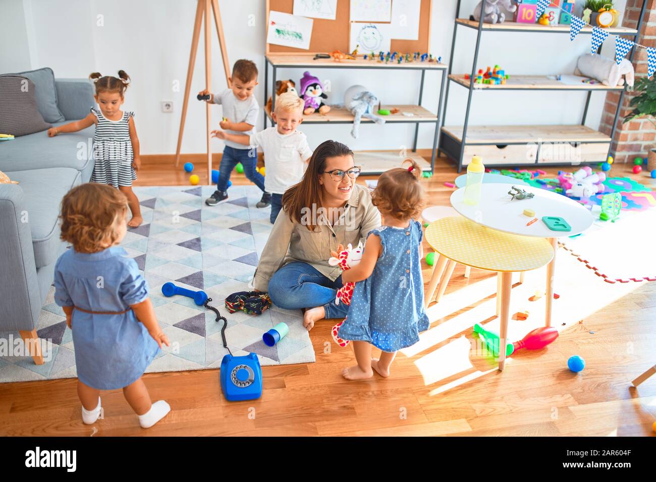 Beautiful teacher and group of toddlers playing around lots of toys at kindergarten Stock Photo ...
