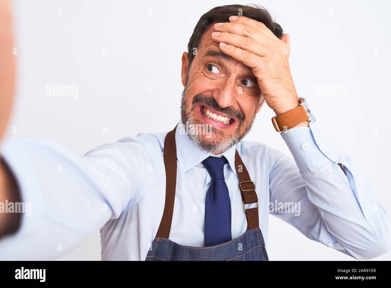 Middle age shopkeeper man wearing apron make selfie over isolated white ...