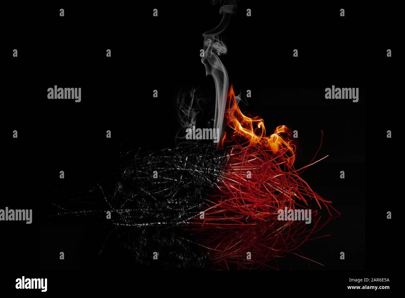 Red chili threads in burning fire ash smoking isolated on black glass ...