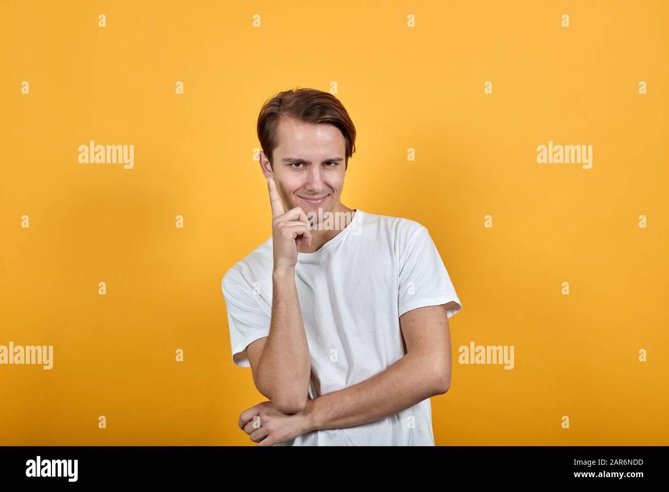 Sly look man in white t-shirt on yellow background holds index finger ...
