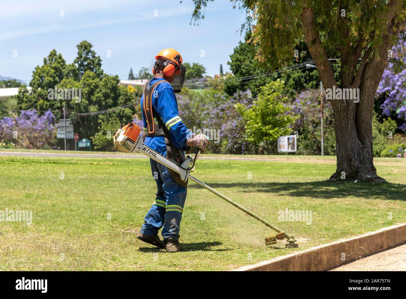 Man wearing protective clothing and safety helmet strimming grass in a ...