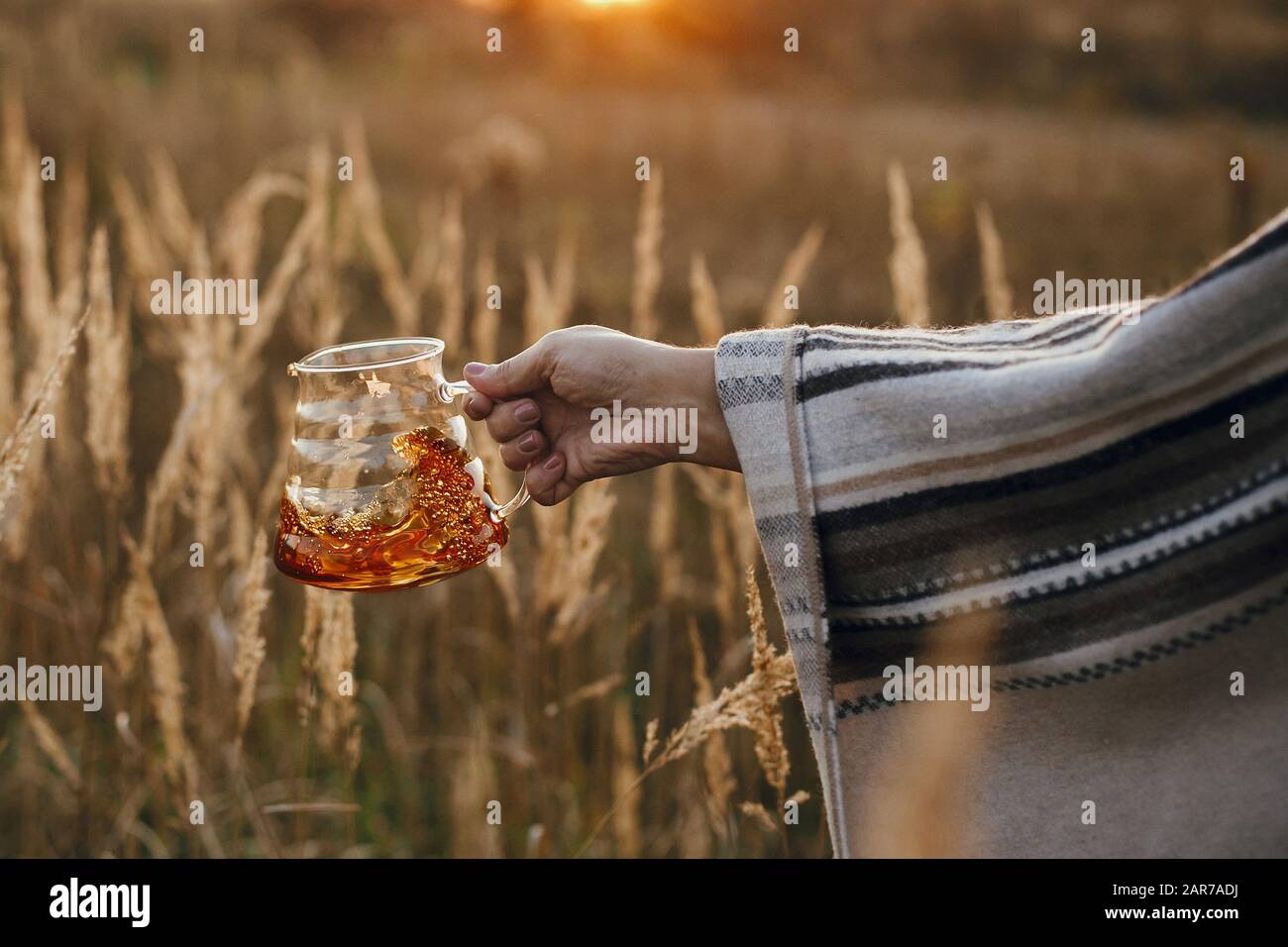 Hand spilling out fresh hot coffee from glass flask in sunny warm light ...