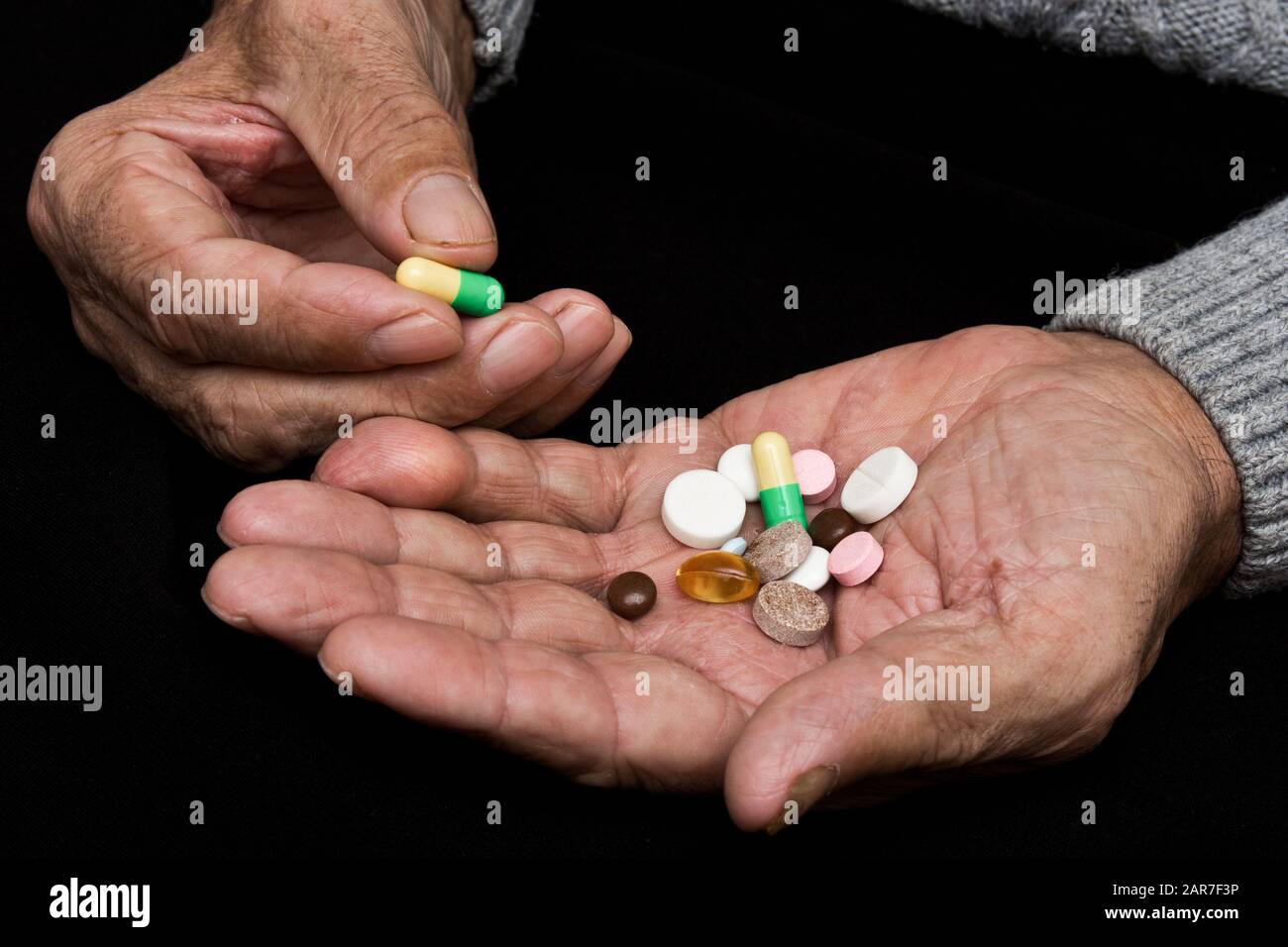 An elderly man holds a lot of colored pills in old hands. Painful old ...
