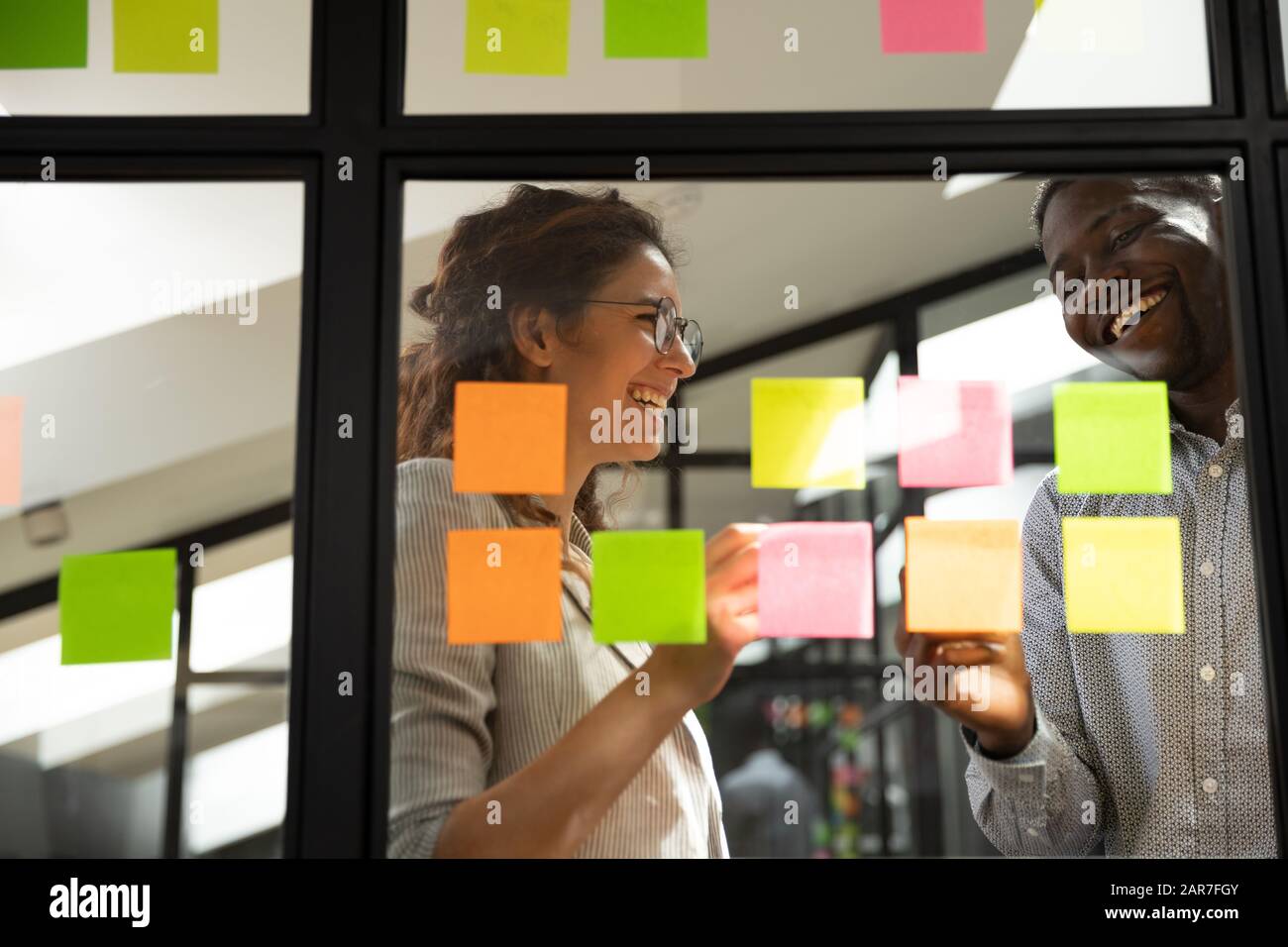 Smiling multiethnic colleagues collaborate project on sticky notes ...