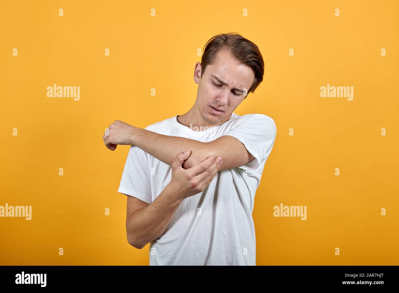 man looks at her elbow, bruised pain. Guy in white t-shirt on yellow ...