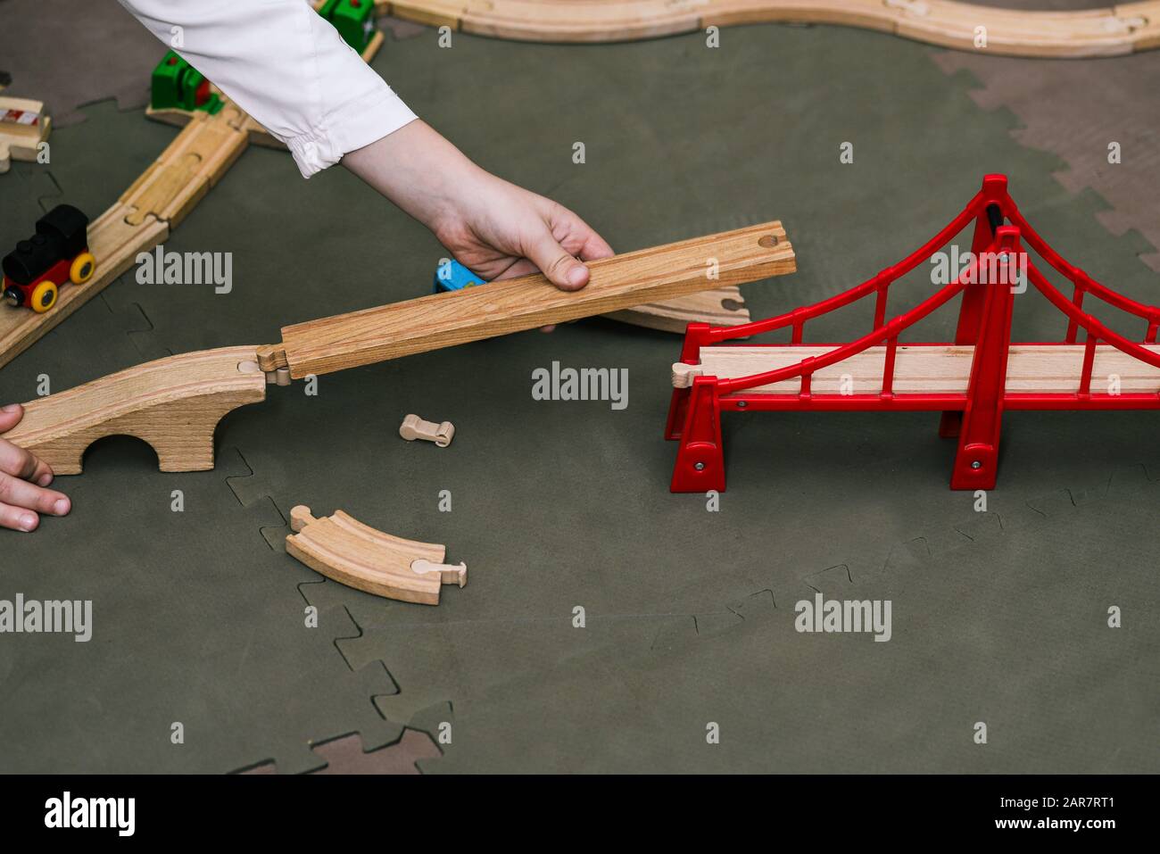 A boy collects a toy railway with a bridge to the floor. Wooden details ...