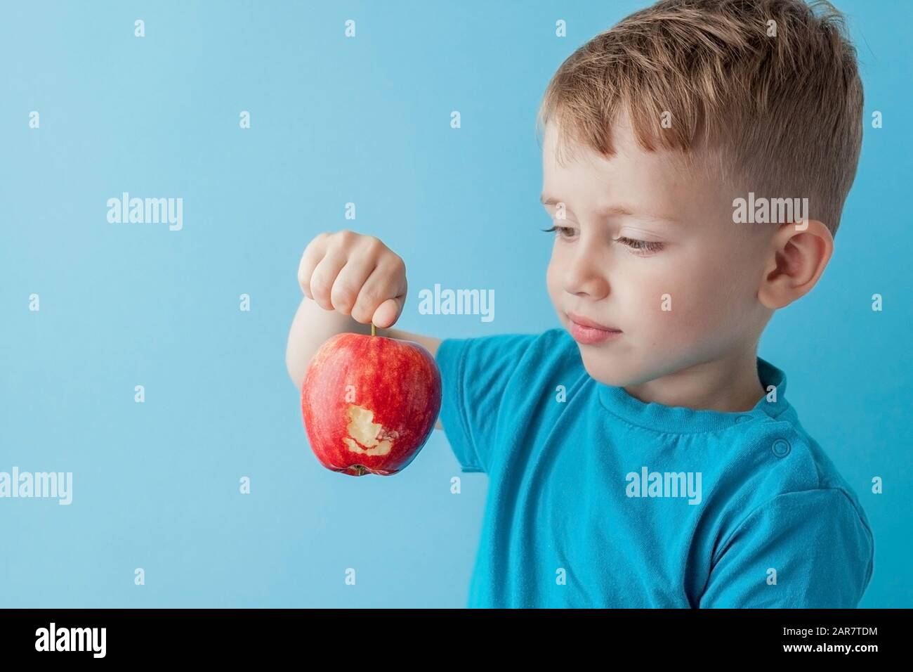 Baby child holding and eating red apple on blue background, food, diet ...