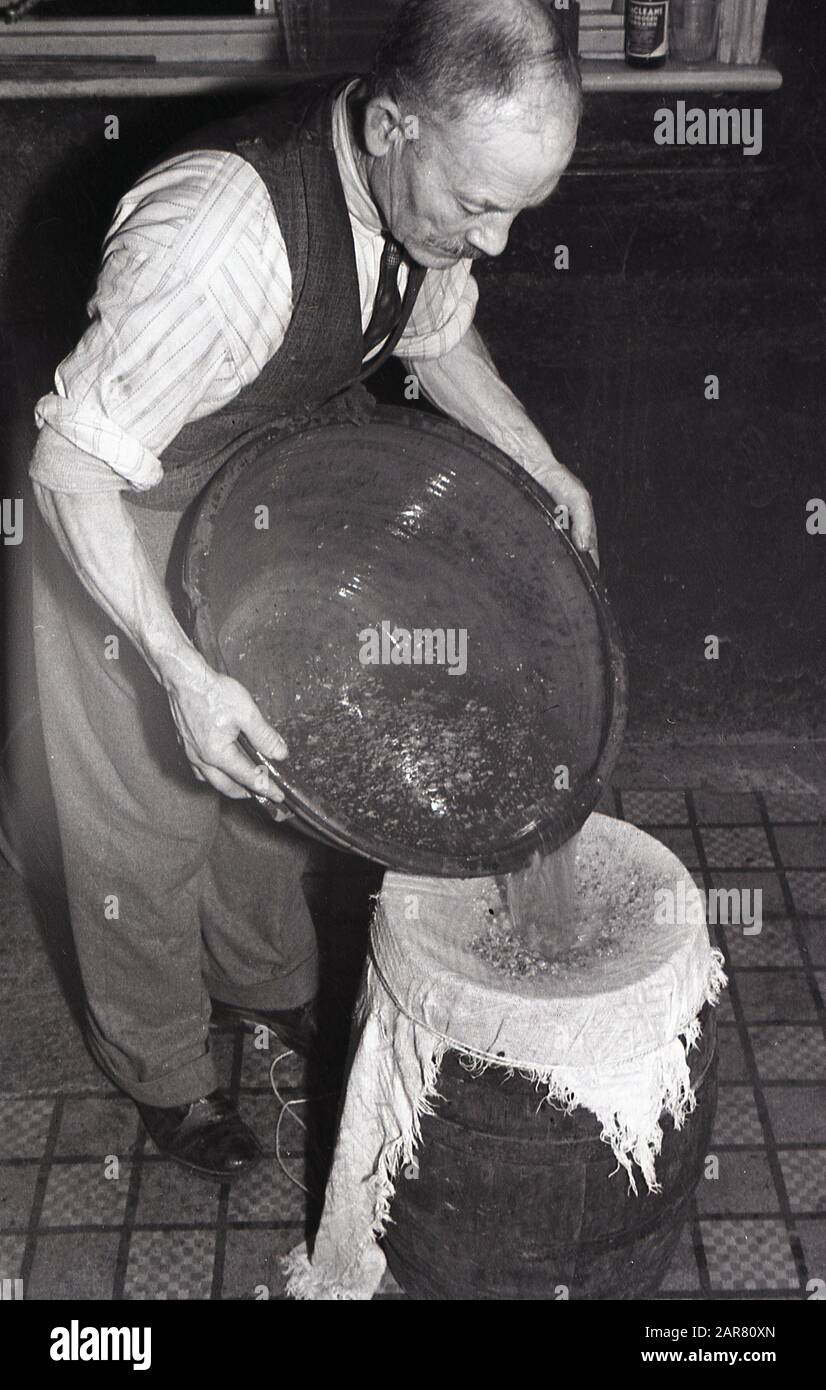 1950s, historical, making mead, a man holding a shallow bowl, pouring ...